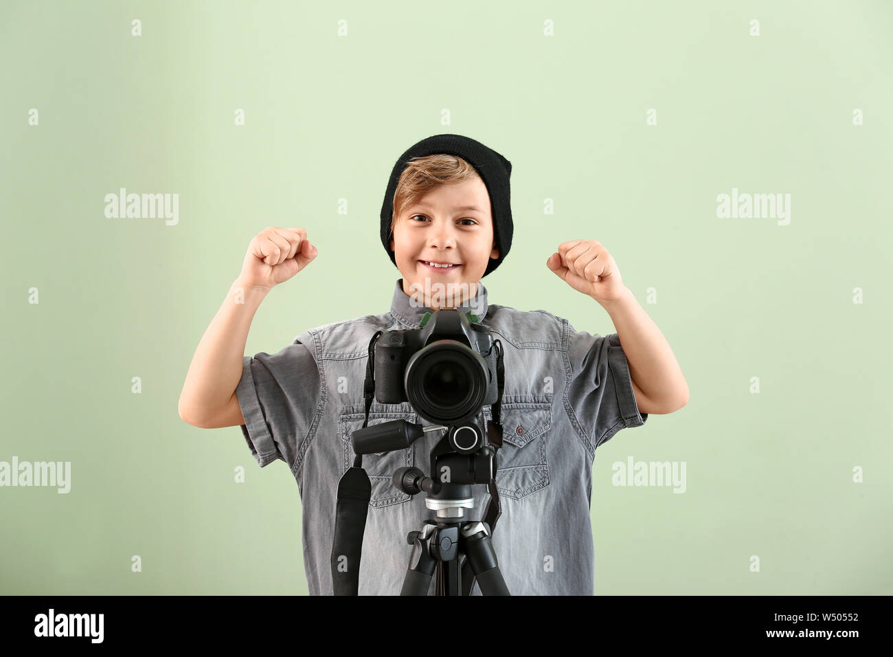 Cute little photographer with professional camera on color background ...