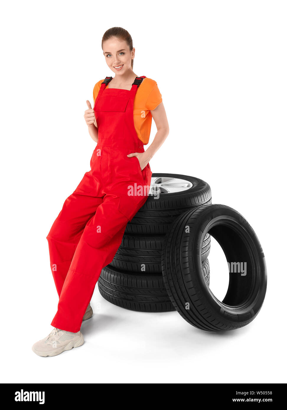 Young female mechanic in uniform with car tires on white background ...