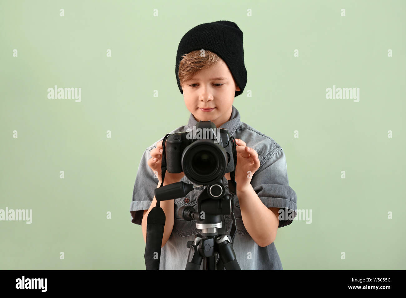Cute little photographer with professional camera on color background ...