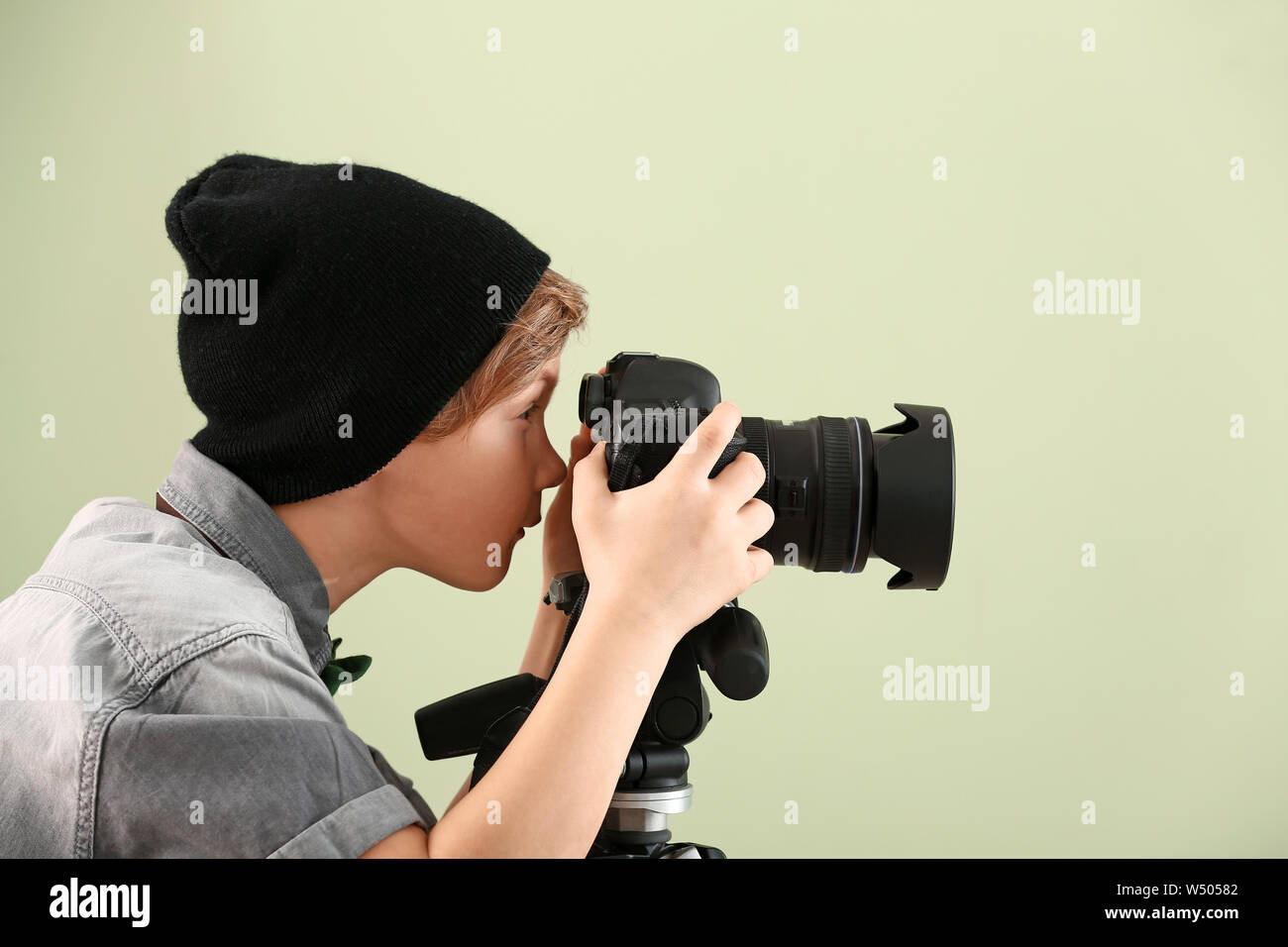 Cute little photographer with professional camera on color background ...