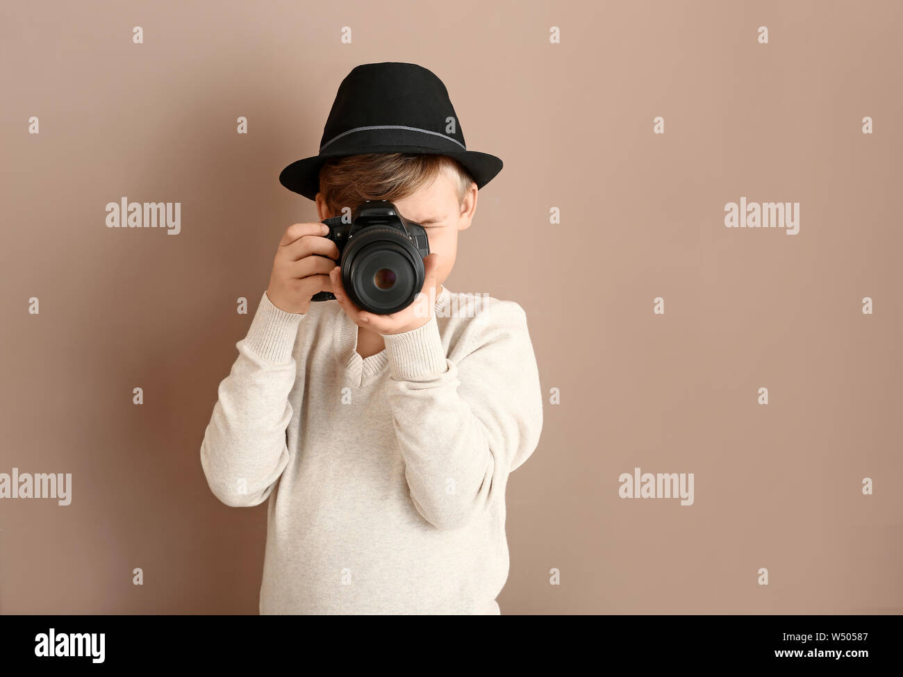 Cute little photographer with professional camera on color background ...