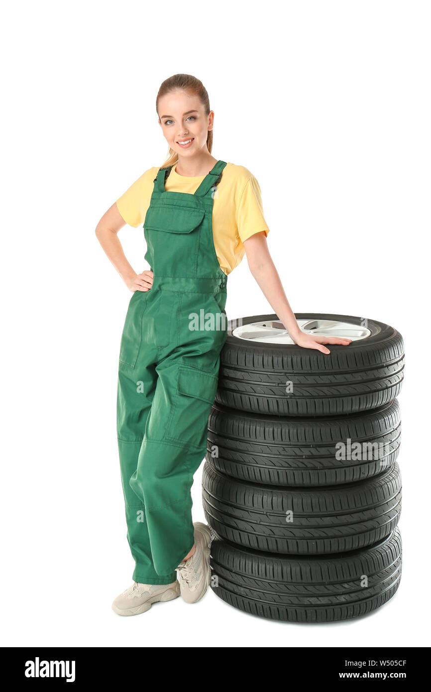 Young female mechanic in uniform with car tires on white background ...