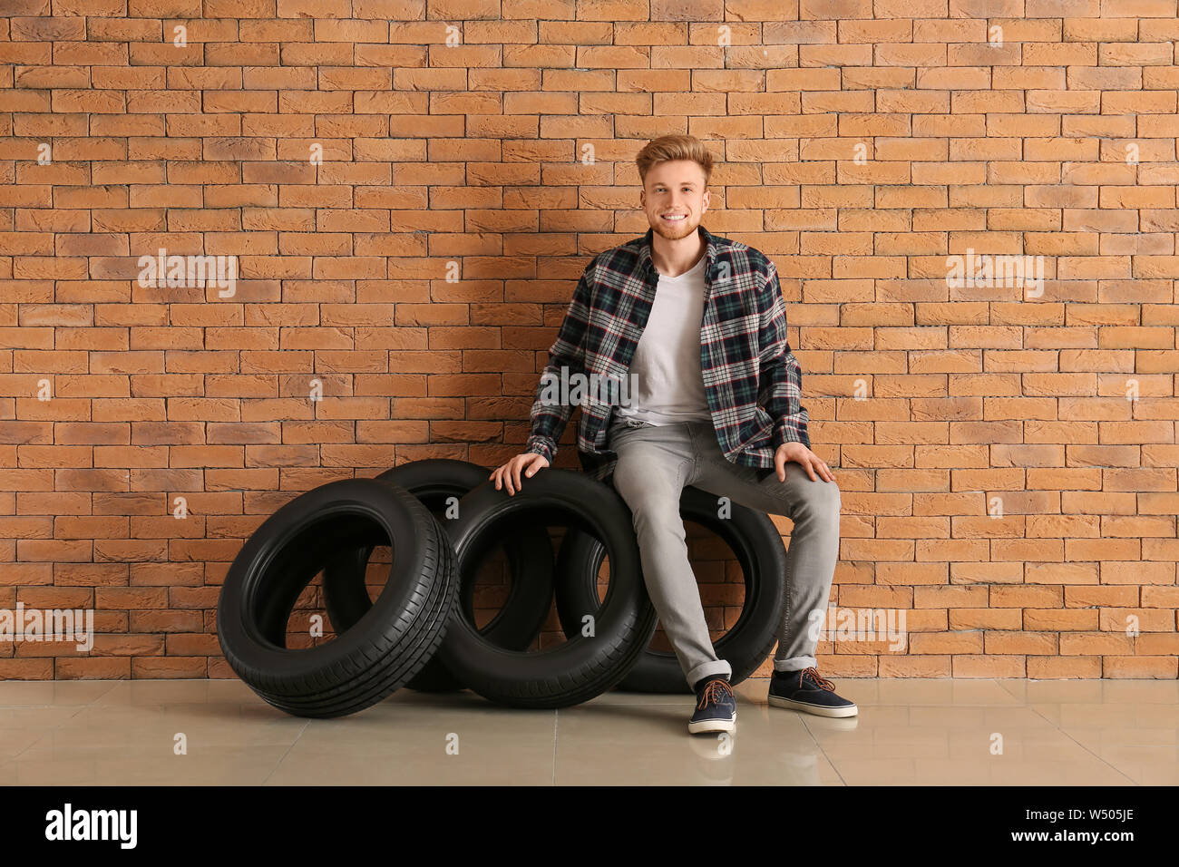 Young man with car tires near brick wall Stock Photo - Alamy