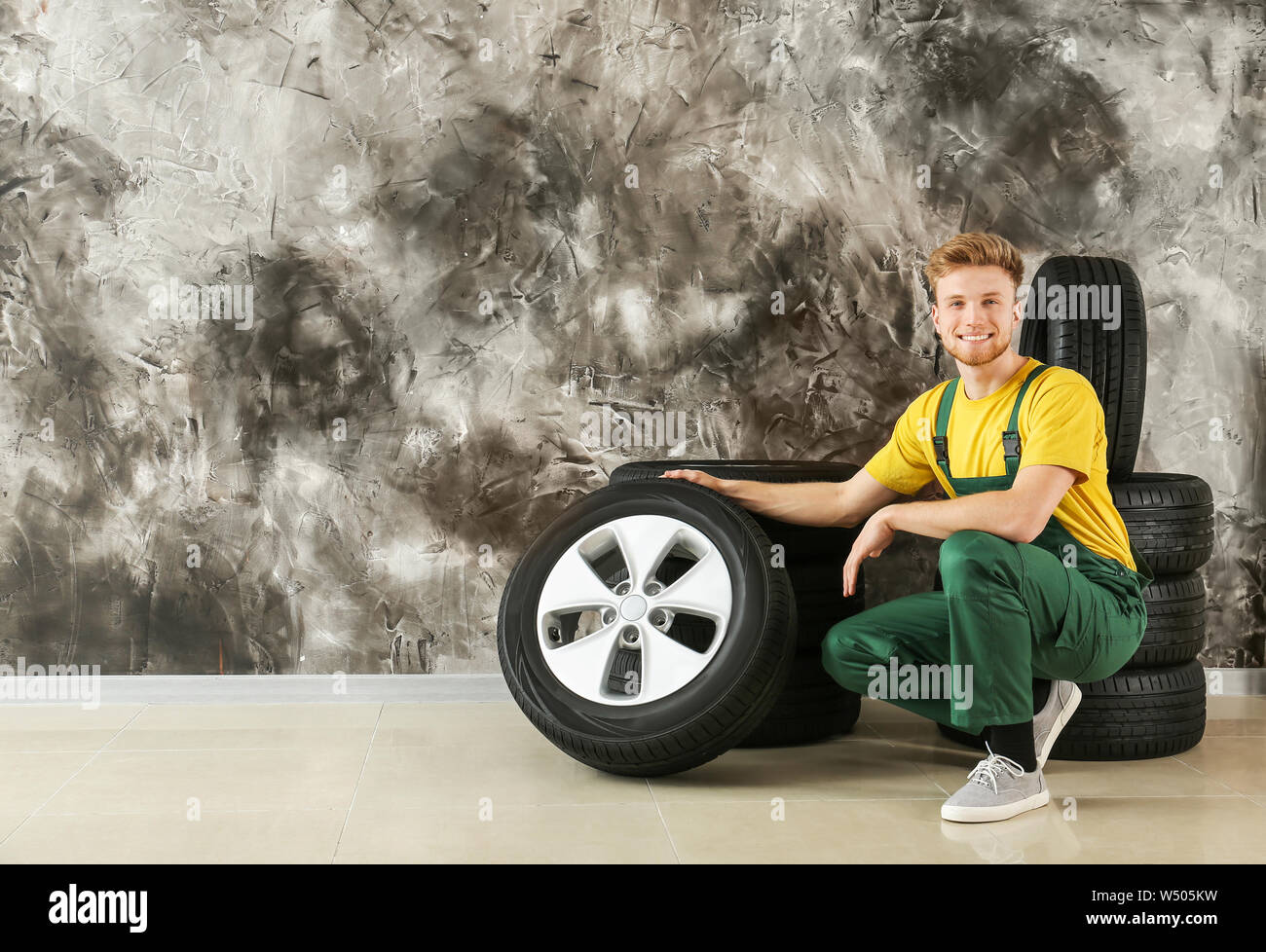 Young male mechanic with car tires near grunge wall Stock Photo - Alamy