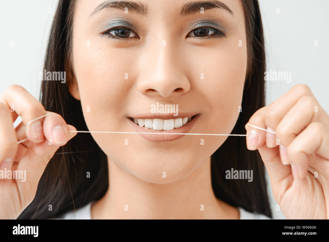 Beautiful Asian woman with dental floss on light background, closeup ...