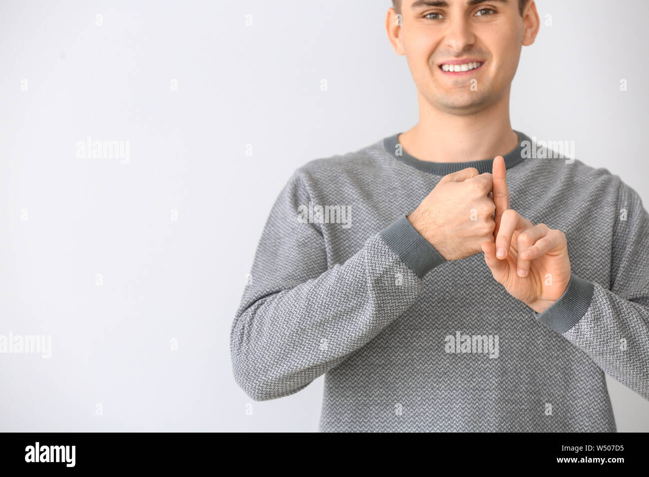 Young deaf mute man using sign language on light background Stock Photo ...