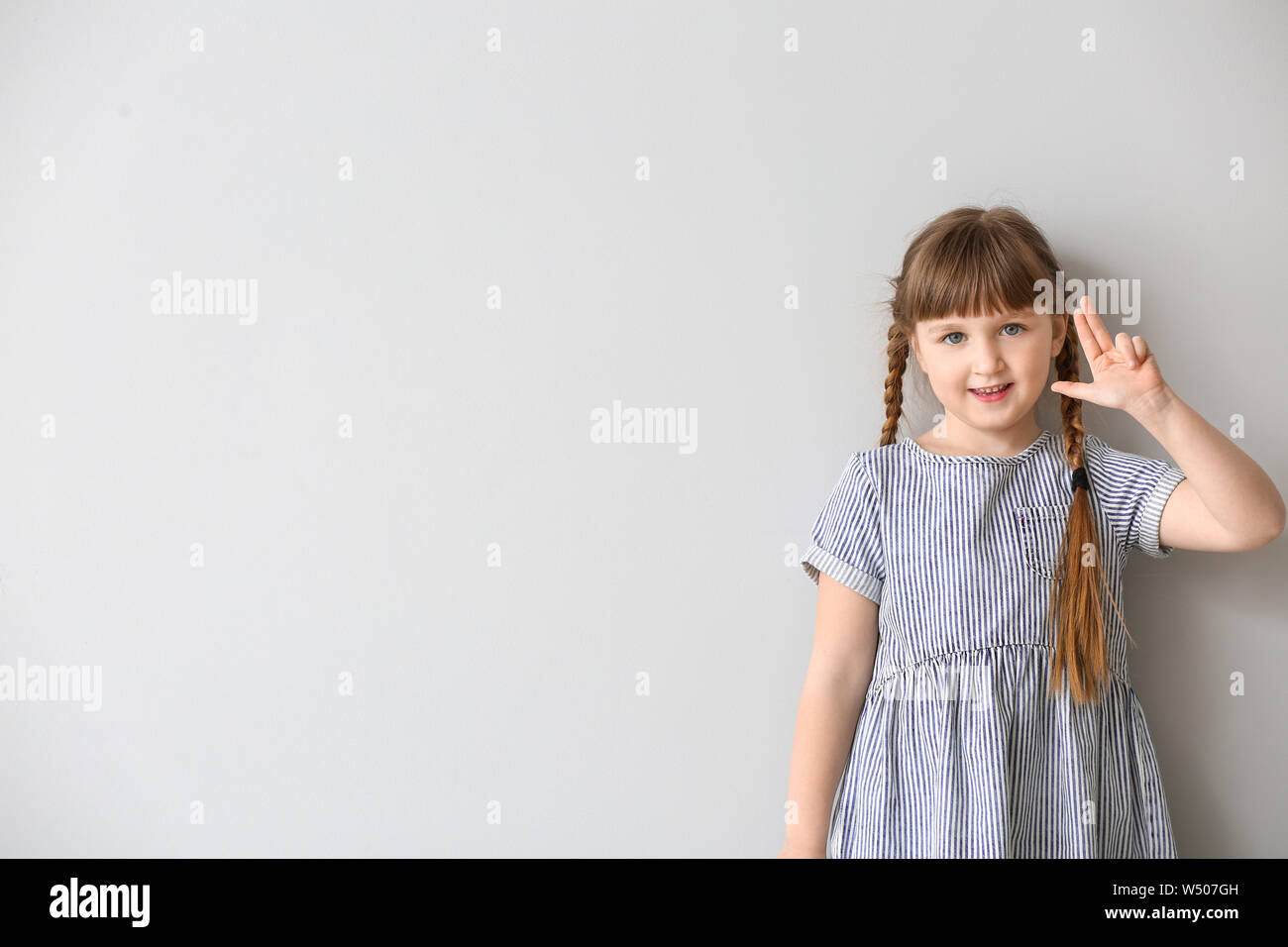 Cute deaf mute girl using sign language on light background Stock Photo ...