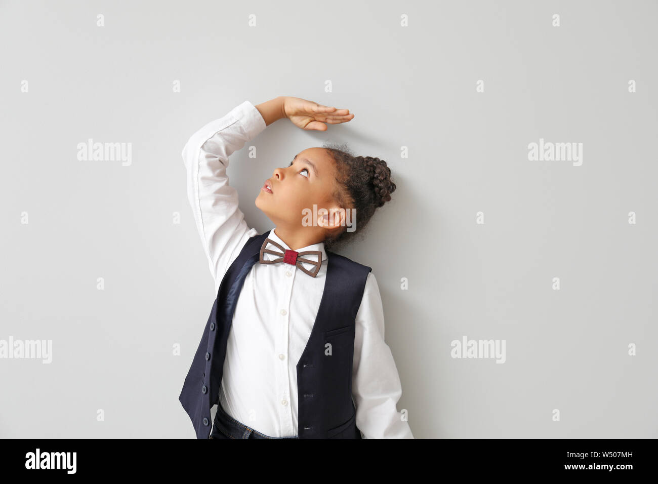 Cute little African-American girl measuring height near light wall ...
