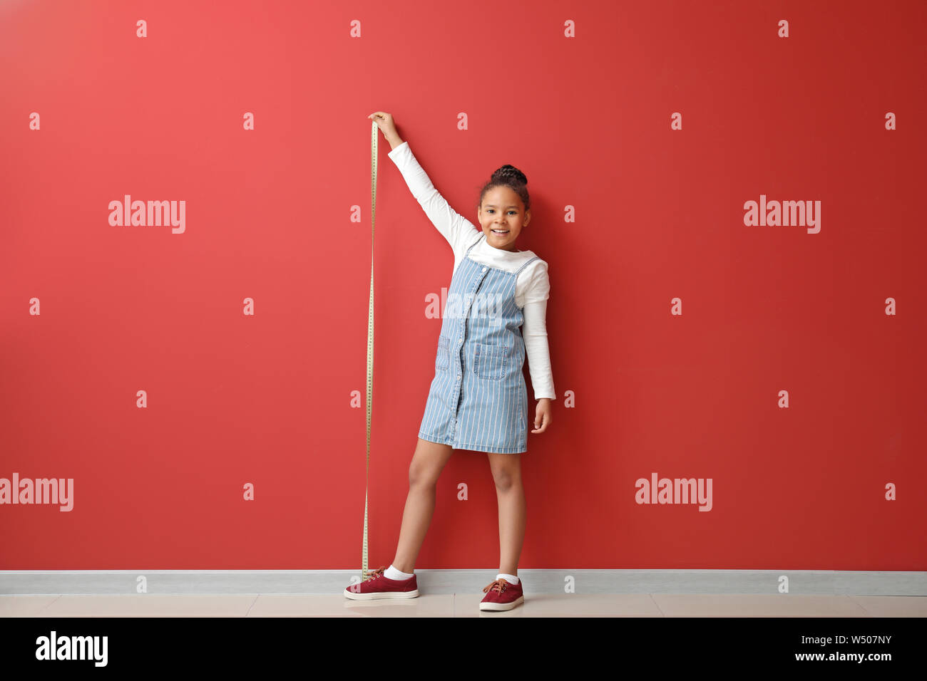 Cute African-American girl measuring height near color wall Stock Photo ...