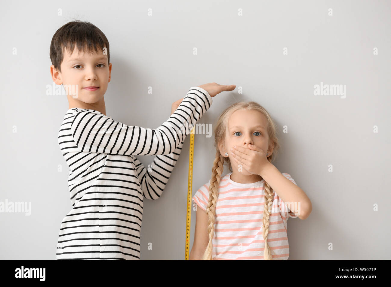 Cute little children measuring height near wall Stock Photo - Alamy