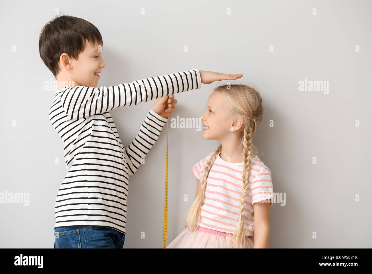 Cute little children measuring height near wall Stock Photo - Alamy