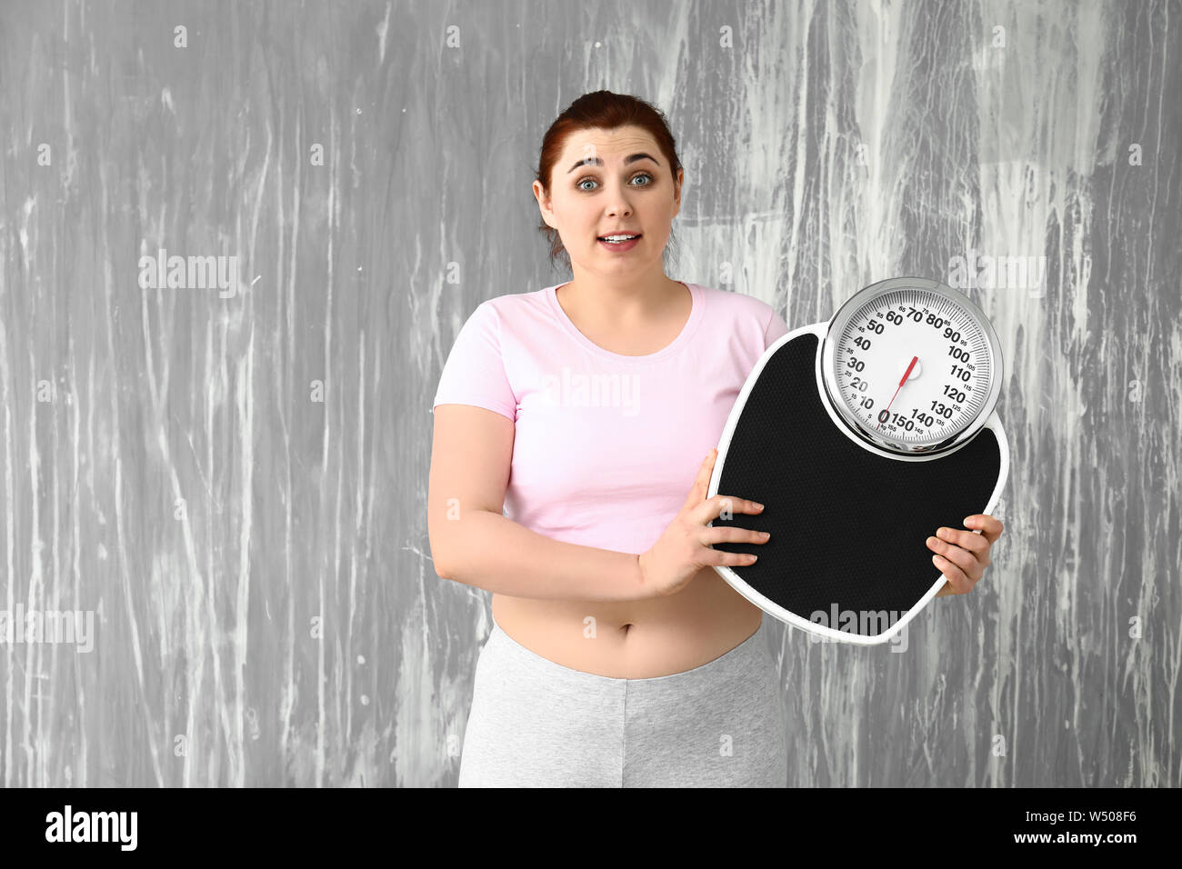 Overweight woman with scales on grey background. Weight loss concept ...