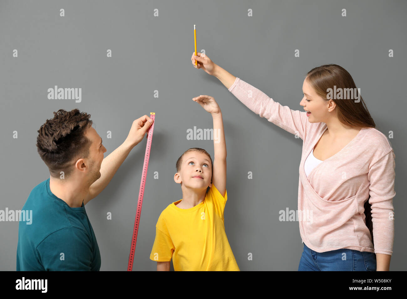 Parents measuring height of their son near grey wall Stock Photo - Alamy
