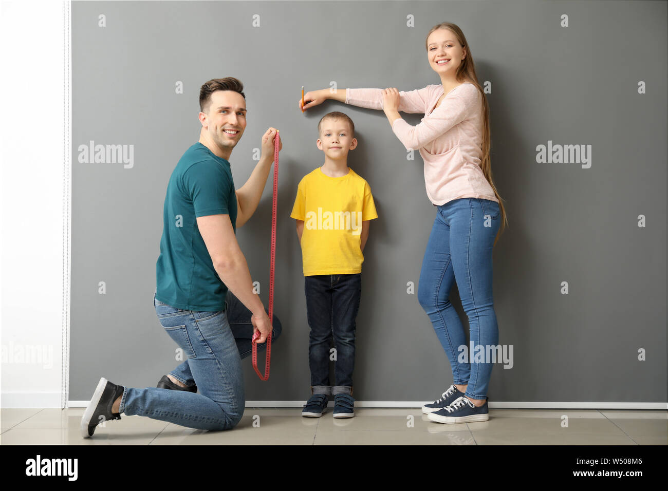 Parents measuring height of their son near grey wall Stock Photo - Alamy