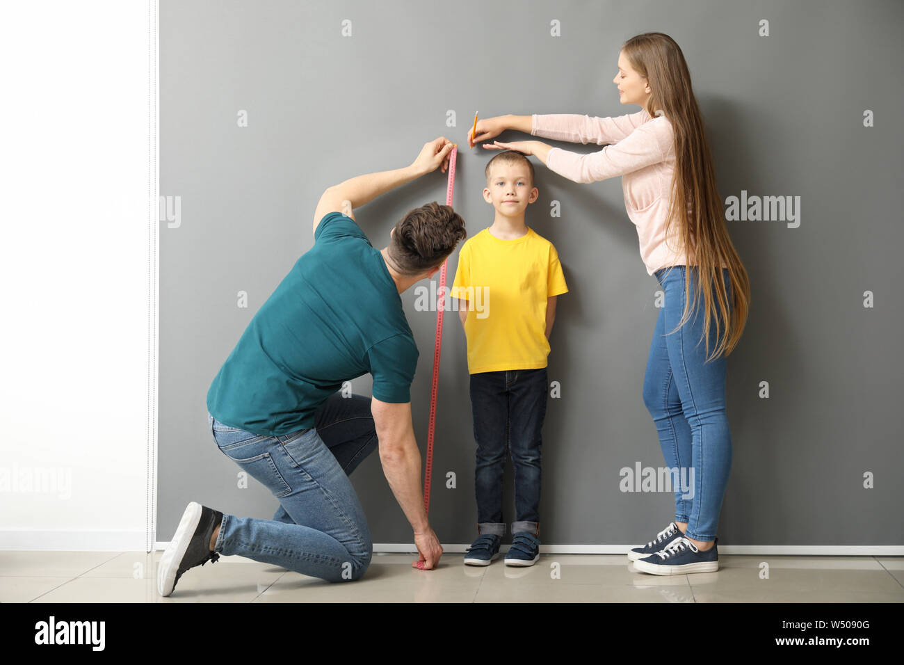 Parents measuring height of their son near grey wall Stock Photo - Alamy