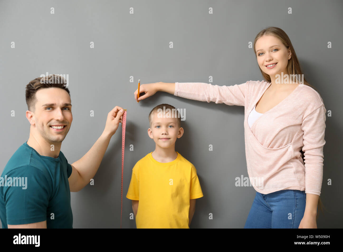 Parents measuring height of their son near grey wall Stock Photo - Alamy