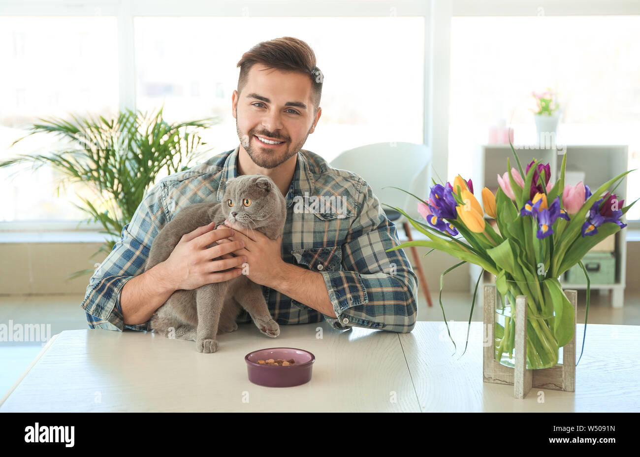 Young man feeding cute funny cat at home Stock Photo - Alamy