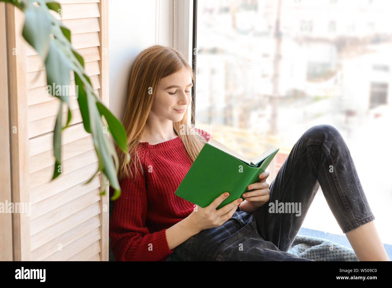 Cute teenage girl reading book on window sill at home Stock Photo - Alamy