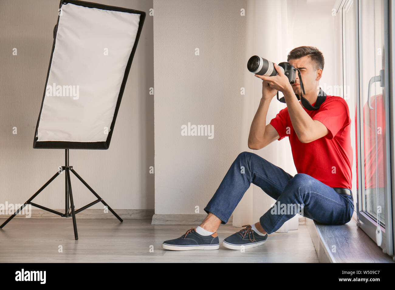 Male photographer sitting on window sill in studio Stock Photo - Alamy