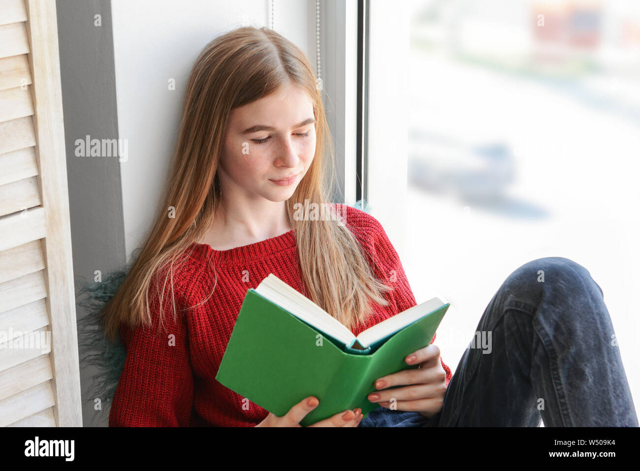 Cute teenage girl reading book on window sill at home Stock Photo - Alamy
