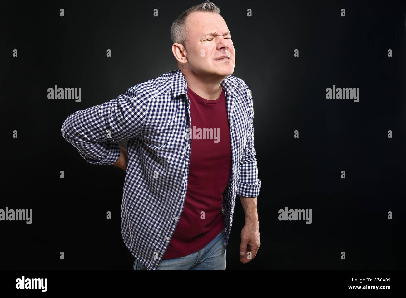 Handsome middle-aged man suffering from back pain on dark background ...