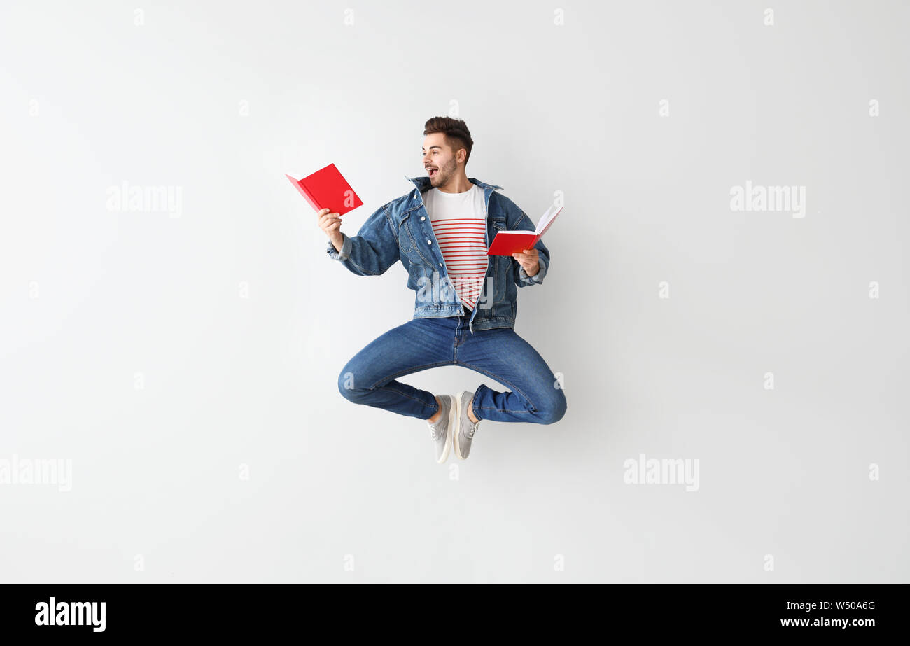 Jumping young man with books on light background Stock Photo - Alamy