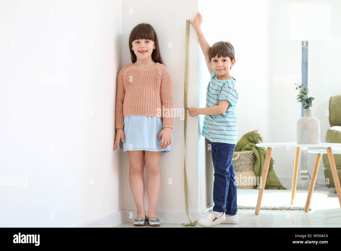 Cute little children measuring height near wall Stock Photo - Alamy