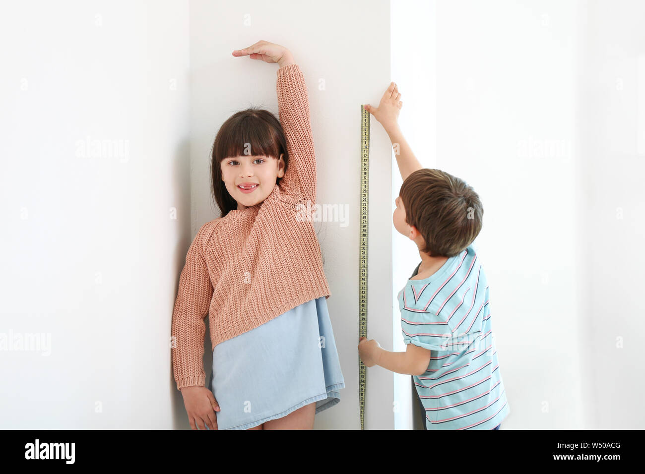 Cute little children measuring height near wall Stock Photo - Alamy