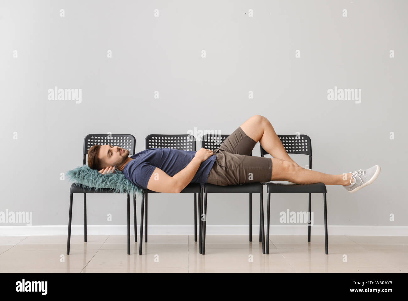 Handsome man sleeping on chairs near grey wall Stock Photo - Alamy