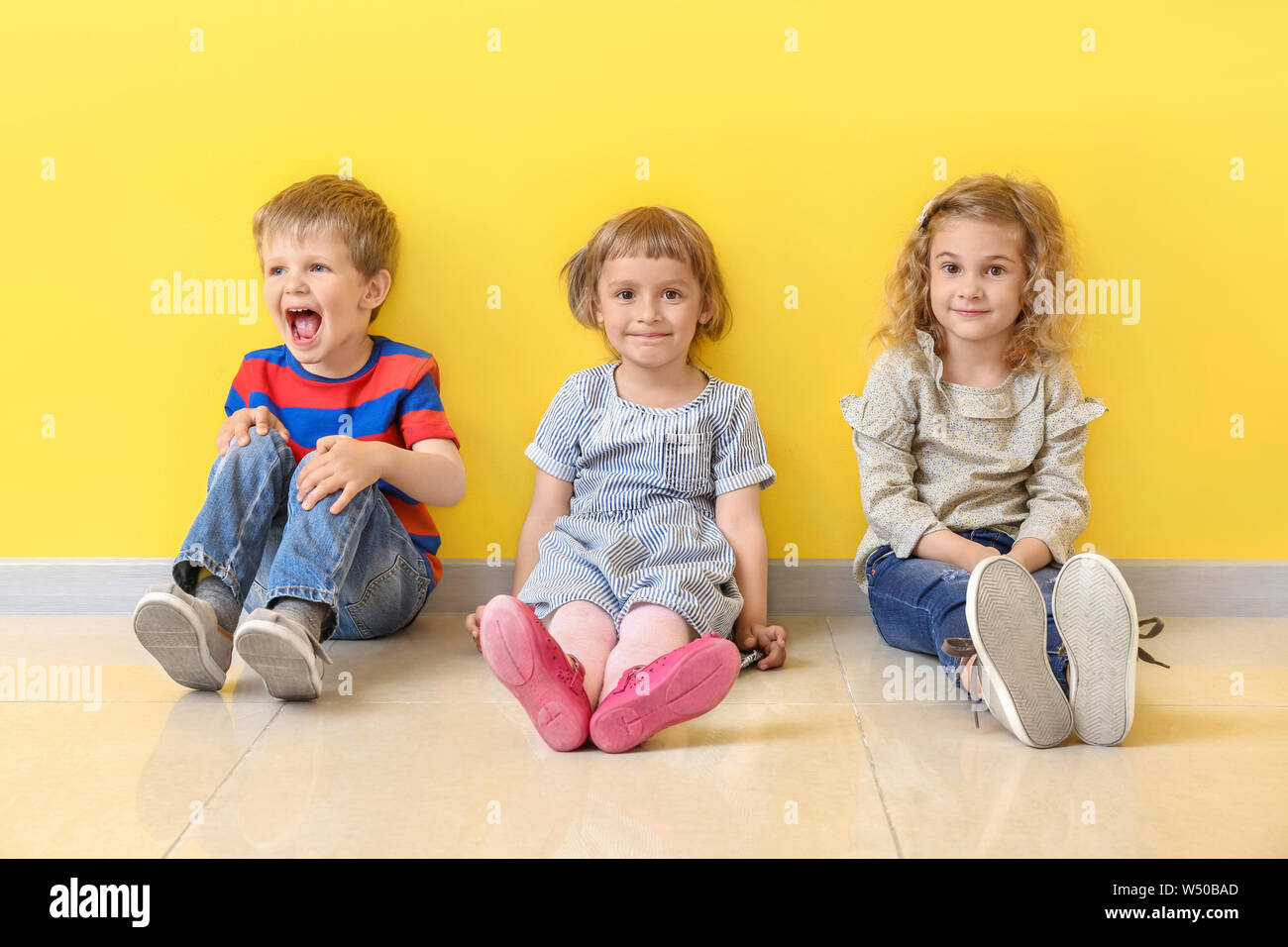 Cute little children sitting near color wall Stock Photo - Alamy