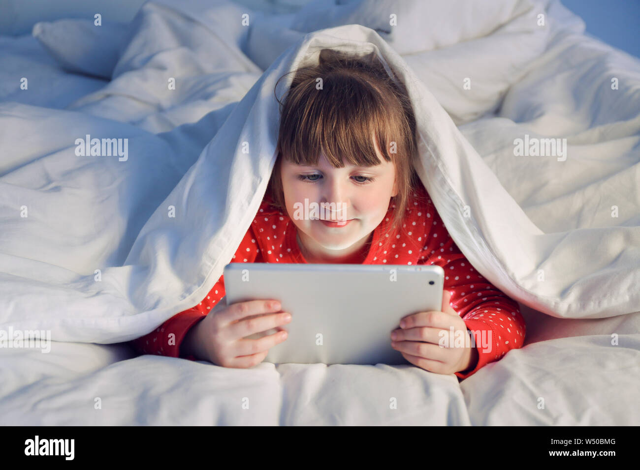 Cute little girl using tablet computer in bed at night Stock Photo - Alamy