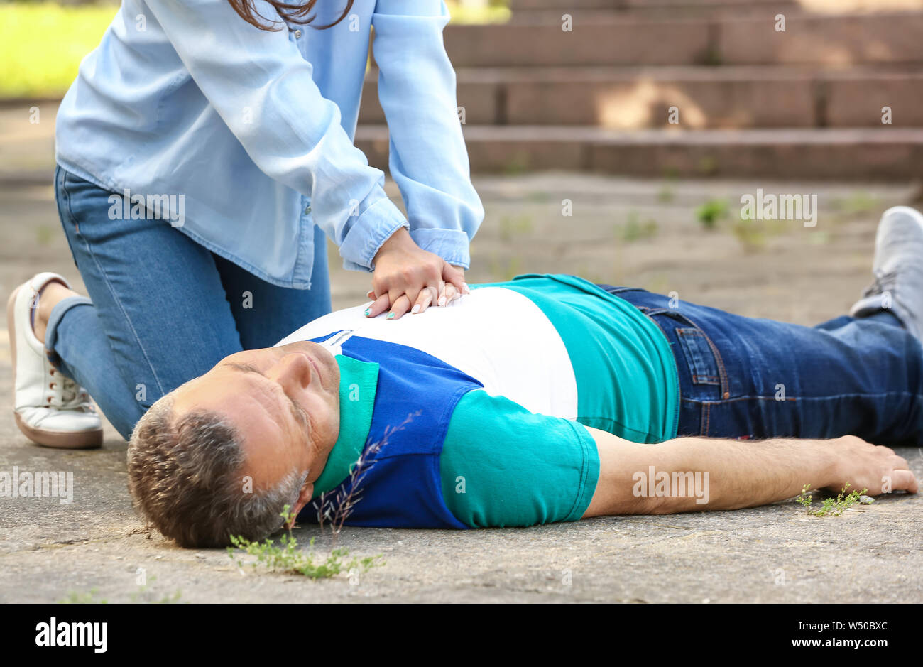 Female passer-by doing CPR on unconscious mature man outdoors Stock ...