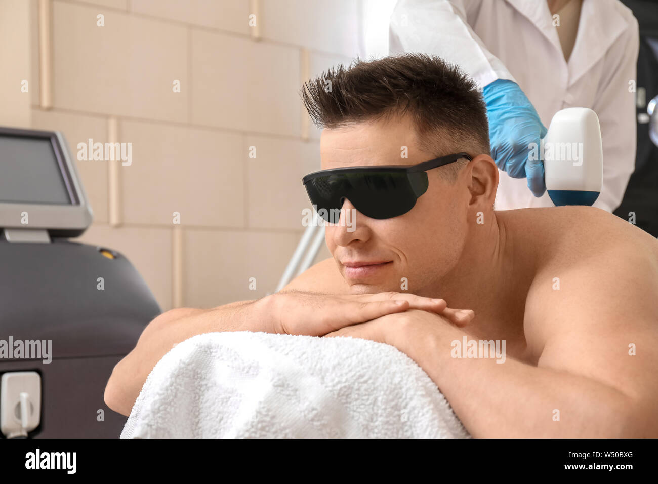 Handsome man undergoing procedure of laser hair removing in beauty ...