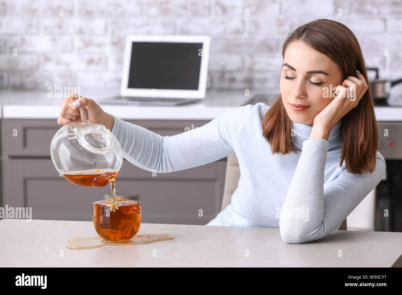 Sleepy young woman spilling tea on kitchen table Stock Photo - Alamy