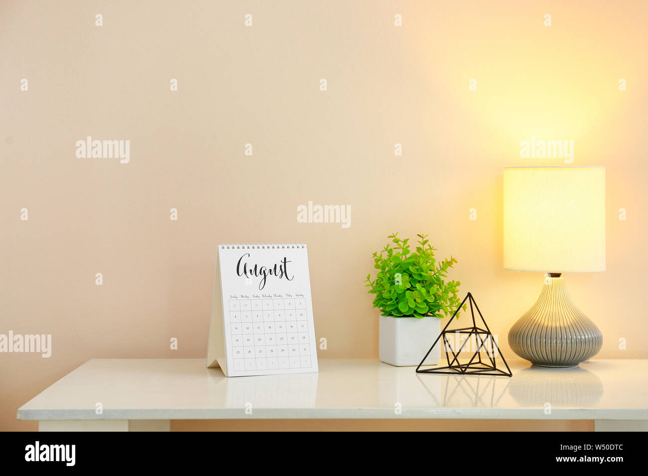 Calendar with lamp and decor on table near light wall in room Stock ...