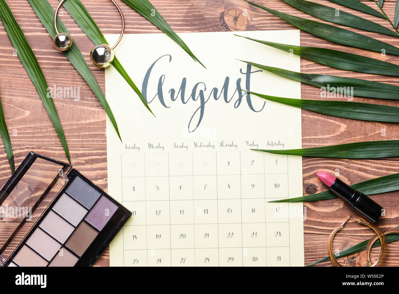 Paper calendar, cosmetics and tropical leaves on wooden background ...