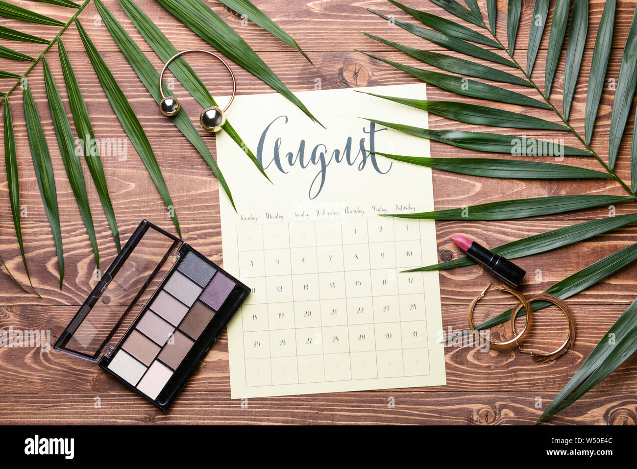 Paper calendar, cosmetics and tropical leaves on wooden background ...