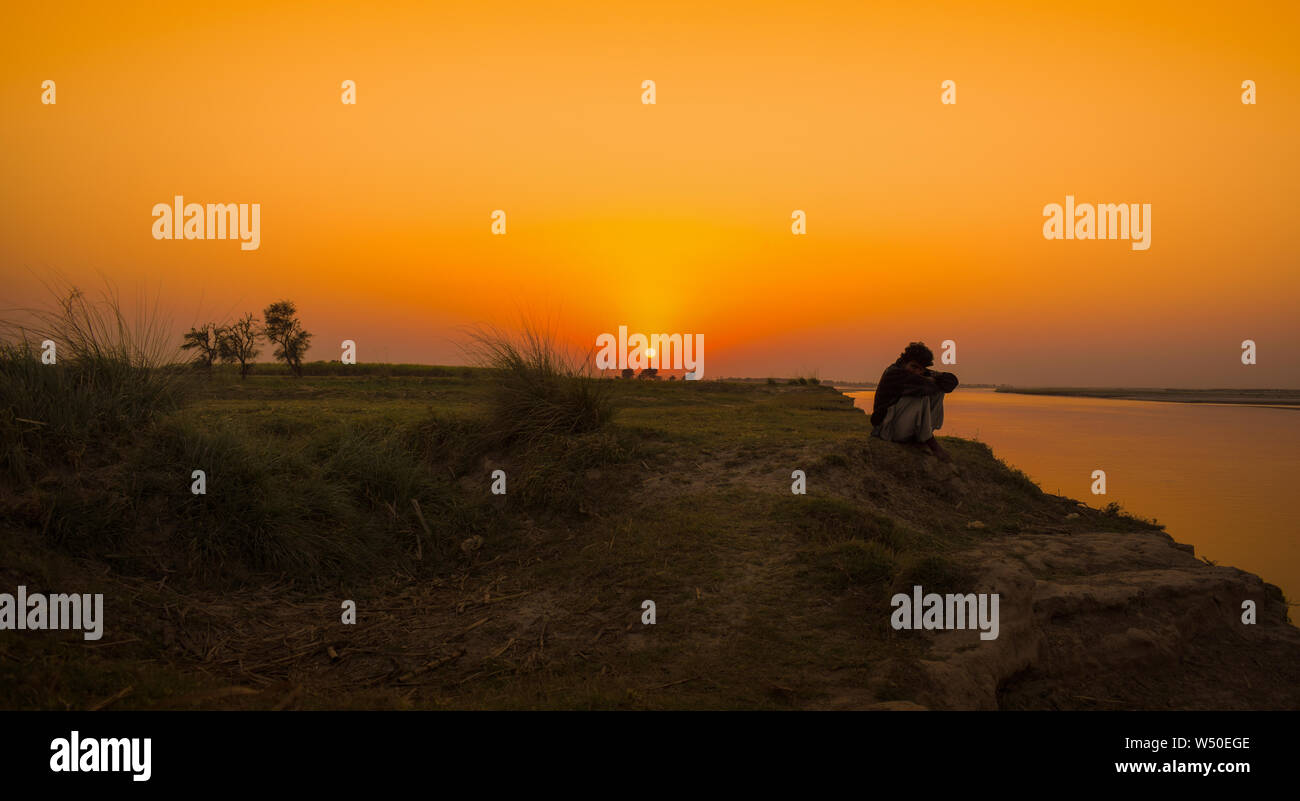 landscape image of a man sitting on a river bank at sunset time,a sad ...