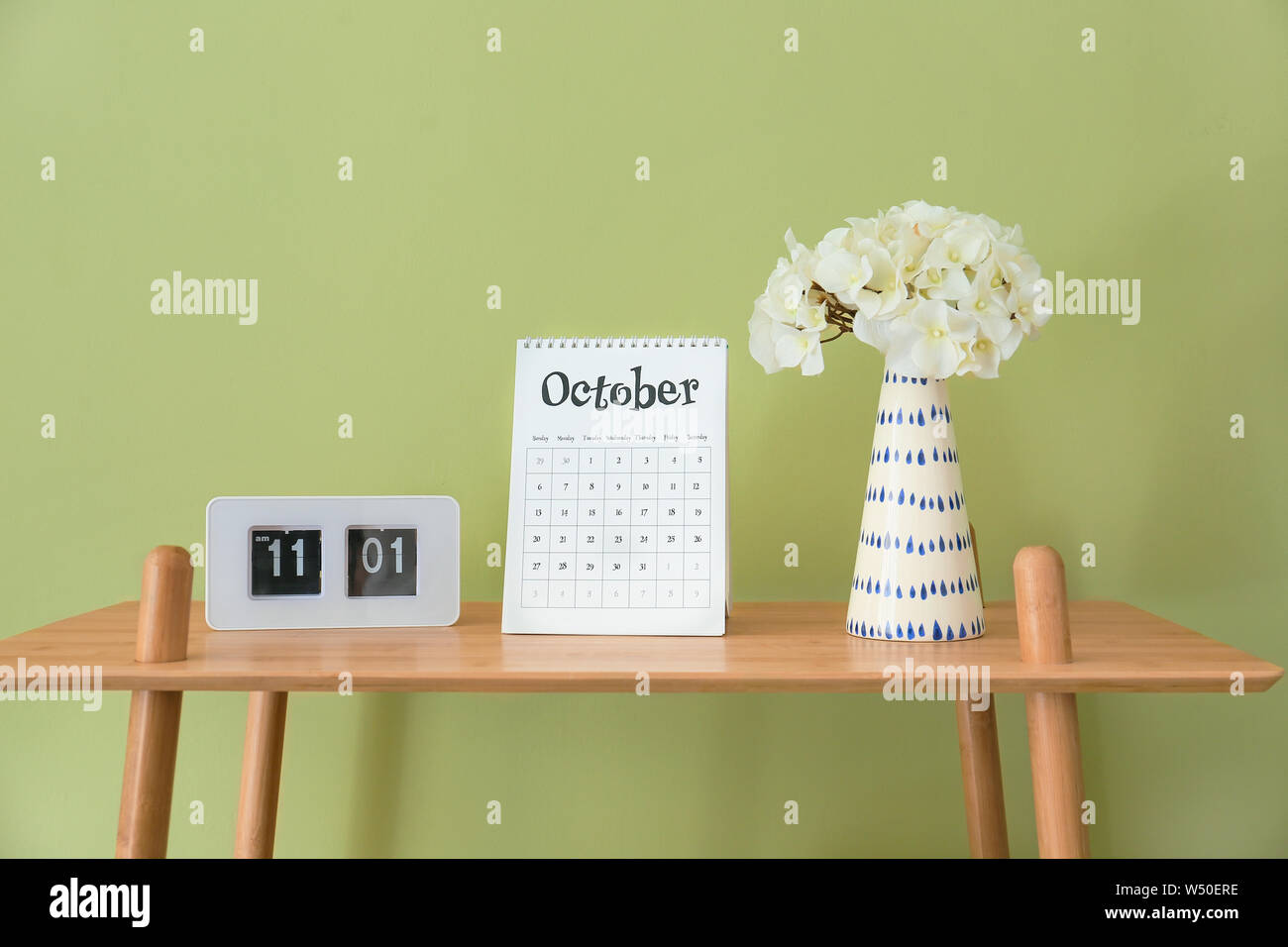 Flip calendar with alarm clock and flowers in vase on table in room ...