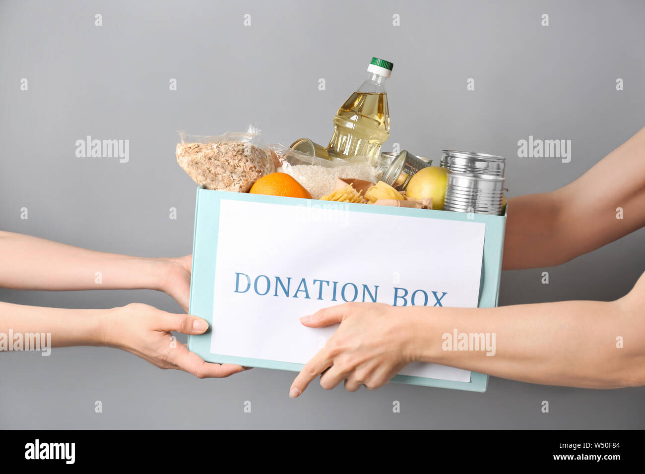 Volunteer giving box with donation food to poor woman against grey ...