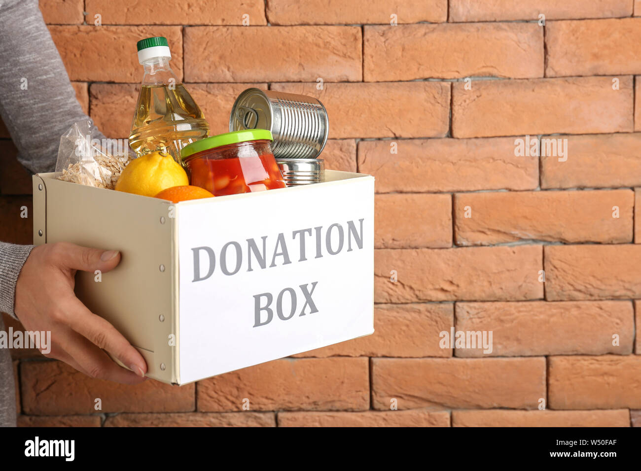 Volunteer holding box with donation box on brick background Stock Photo ...