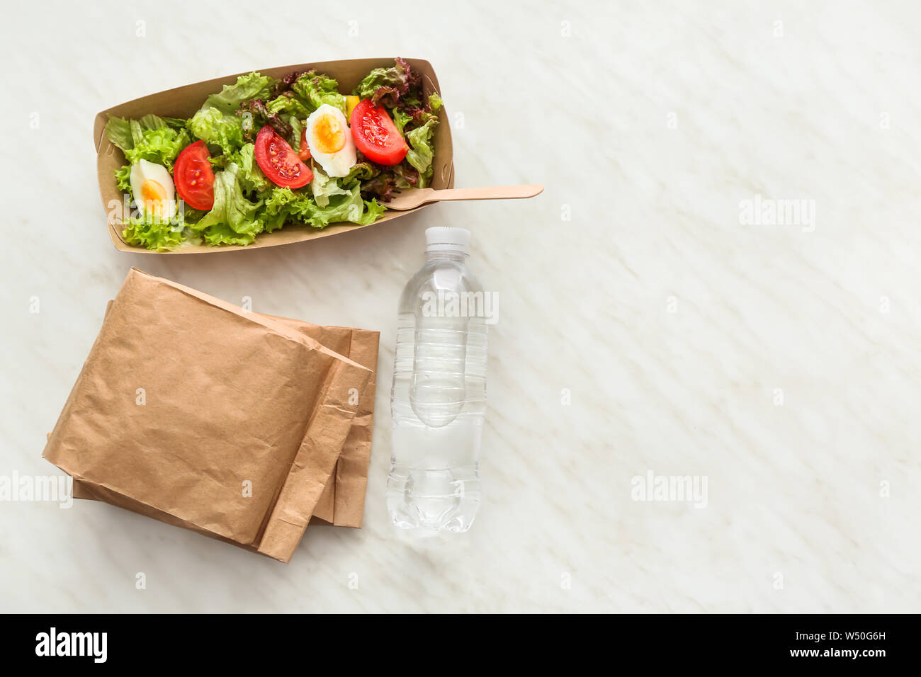 Bottle of water, paper box and bags with delicious food on light ...