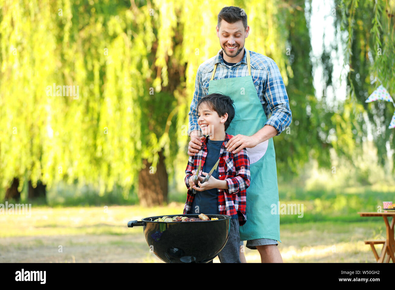 Little boy with father cooking tasty food on barbecue grill outdoors ...