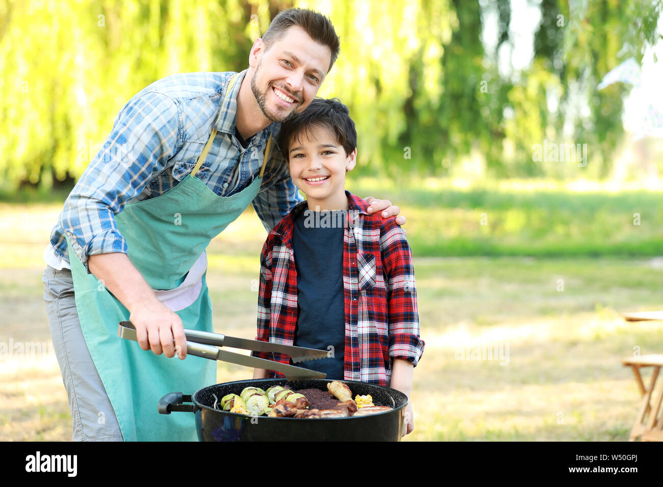 Little boy with father cooking tasty food on barbecue grill outdoors ...
