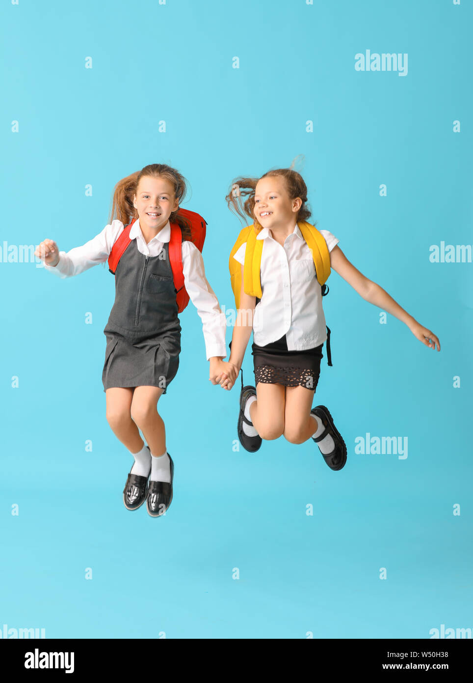 Cute jumping schoolgirls on color background Stock Photo - Alamy