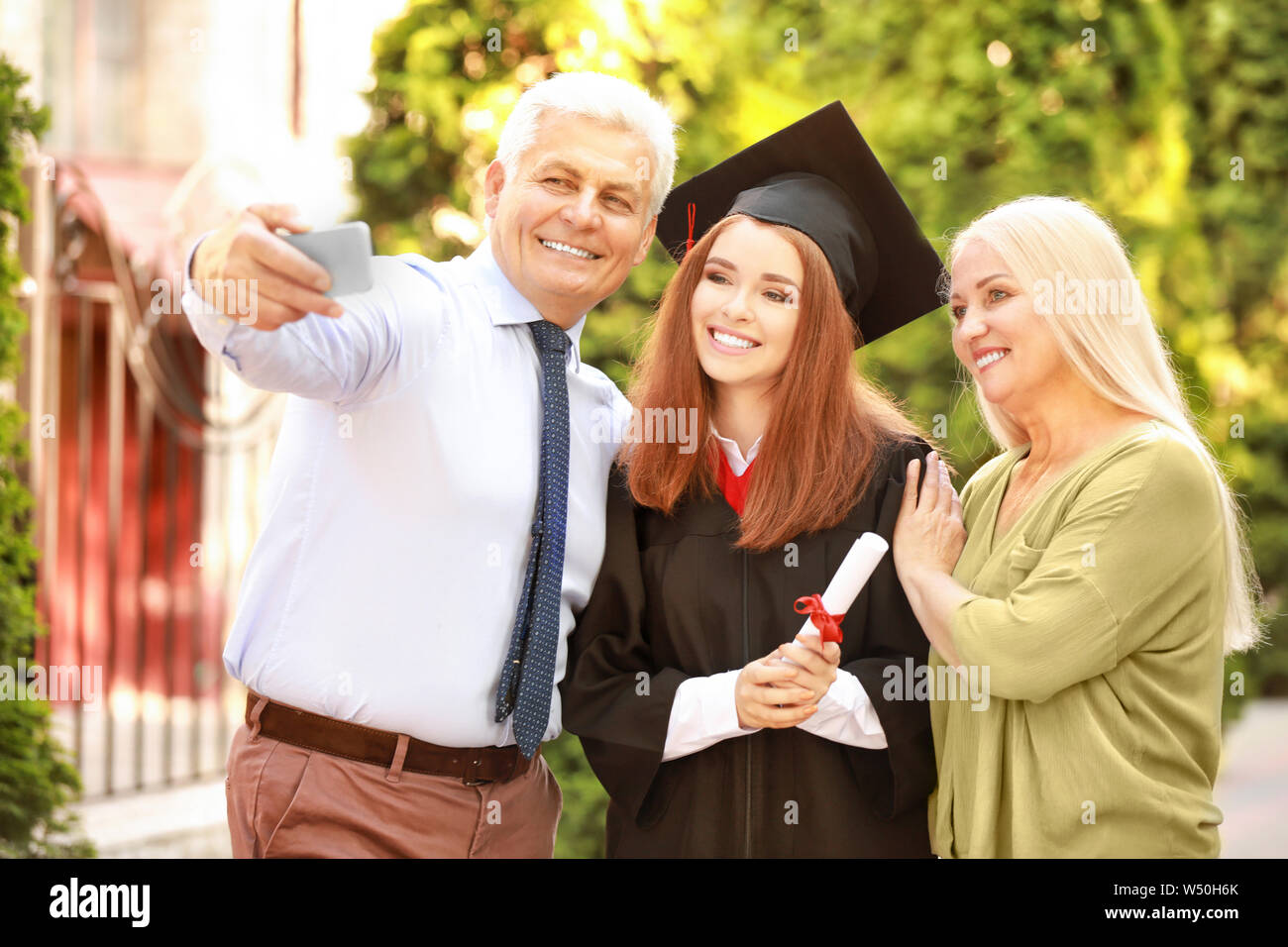 Happy young woman with her parents taking selfie on graduation day ...