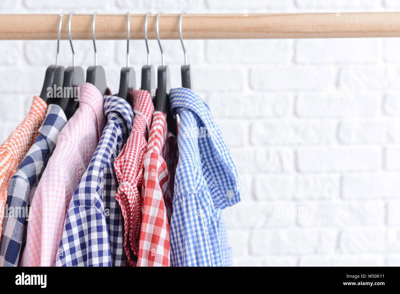 Rack with hanging clothes against white brick wall Stock Photo - Alamy