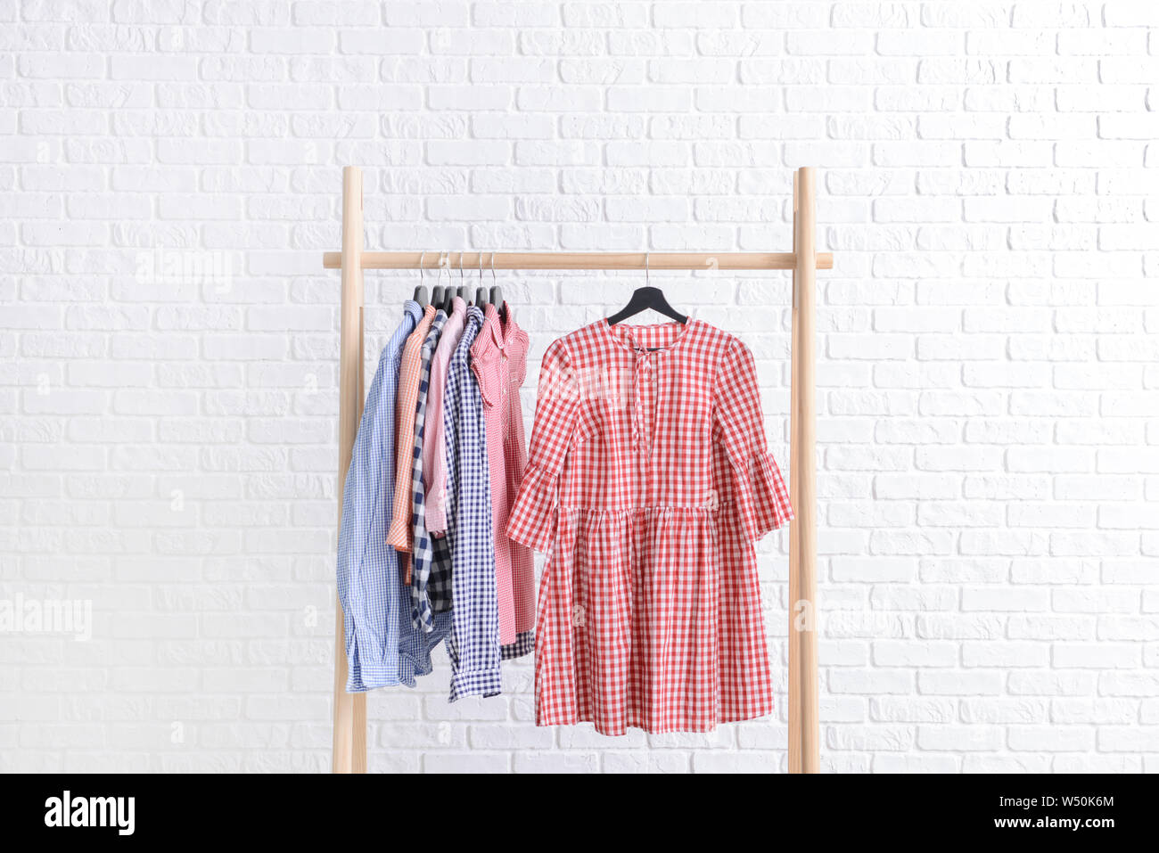 Rack with hanging clothes against white brick wall Stock Photo - Alamy