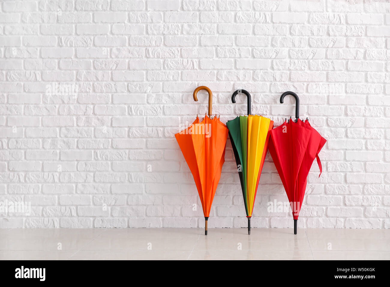 Stylish umbrellas near white brick wall Stock Photo - Alamy