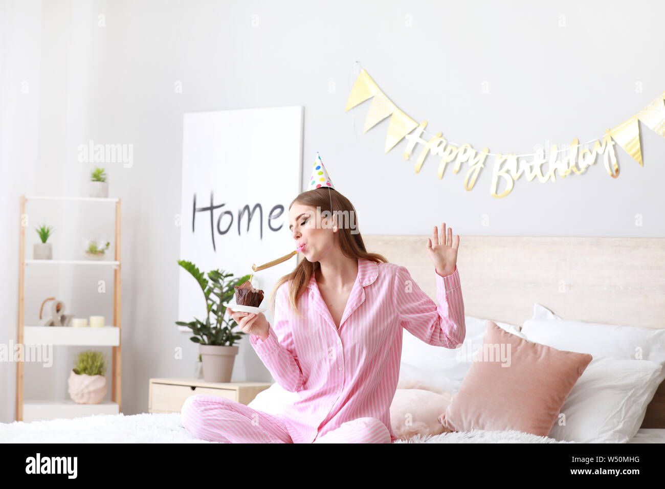 Happy woman with Birthday cake and party whistle in bedroom at home ...